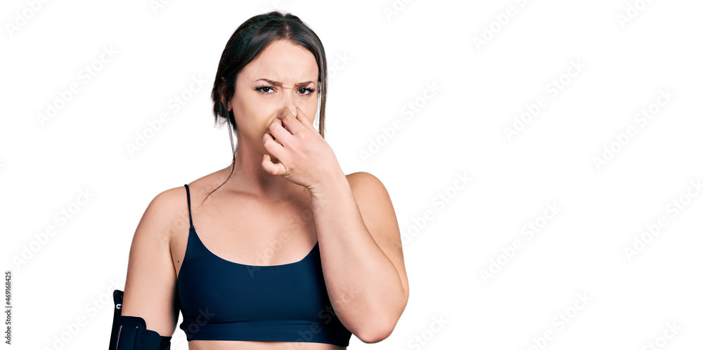 Young hispanic woman wearing sportswear smelling something stinky and ...