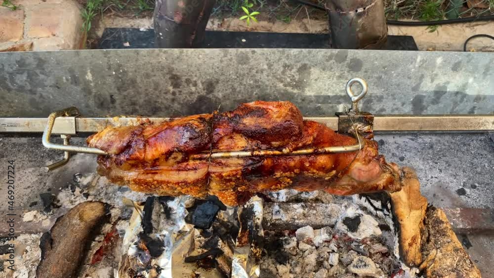 Roasting suckling pig on a spit metal rotating stick over hot fire ...