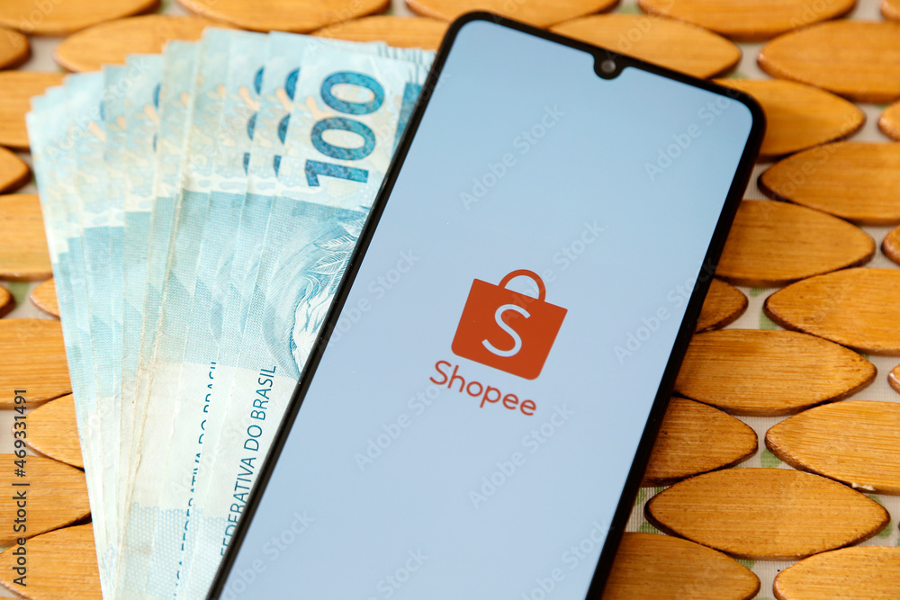 Shopee logo on mobile screen and Brazilian money bills Stock Photo ...