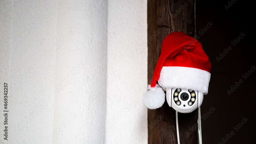 White CCTV camera in red Santa Claus hat. Outdoor video surveillance ...