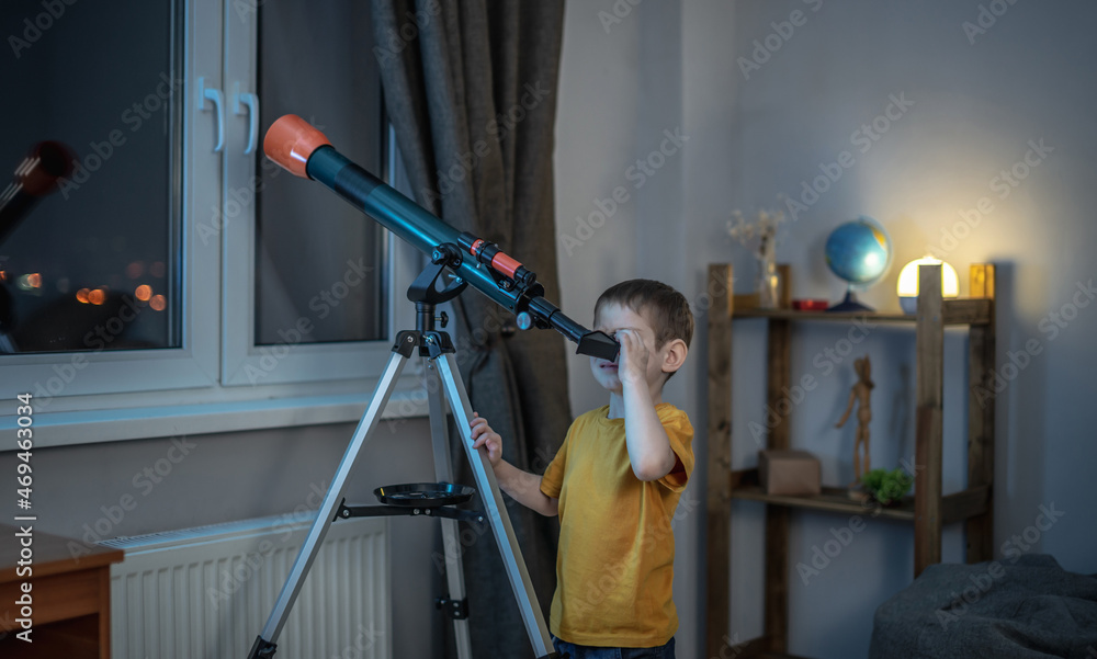 Cute boy is looking through a telescope at the night starry sky ...