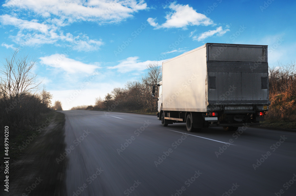Box truck driving fast on a countryside road with trees against a sky ...