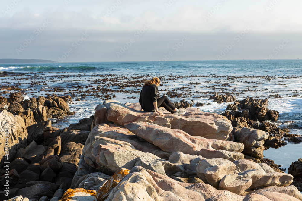 Teenage girl walking across jagged rocks, exploring rock pools by the ...
