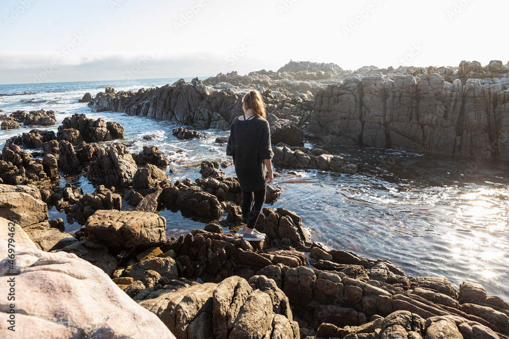 Teenage girl walking across jagged rocks, exploring rock pools by the ...