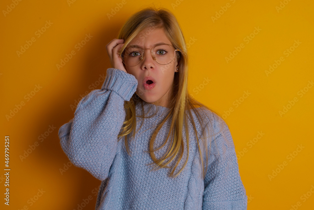 Embarrassed caucasian kid girl wearing blue knitted sweater over yellow ...