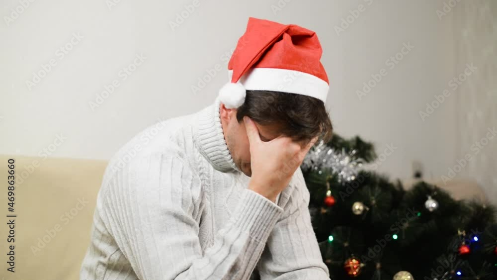 Loneliness in Christmas celebration. Sad, angry, young man in Santa hat ...