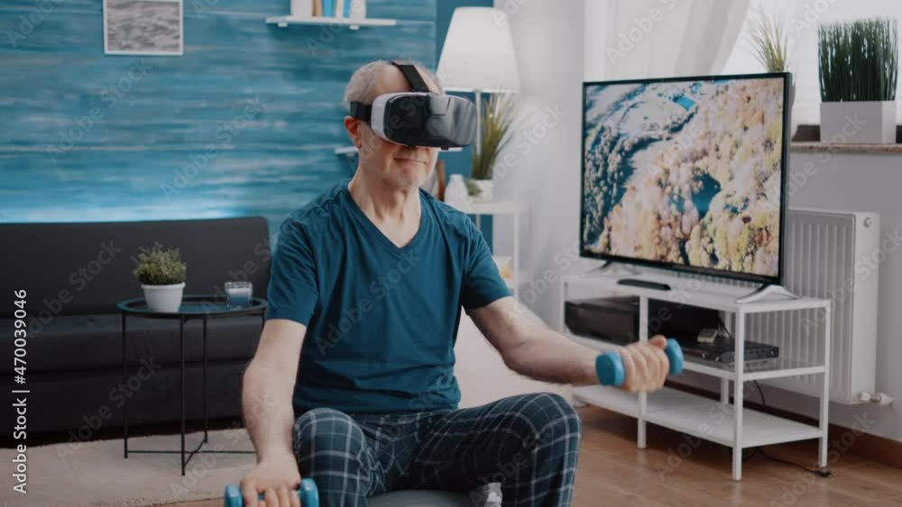 Pensioner using vr glasses to do physical exercise with dumbbells while ...