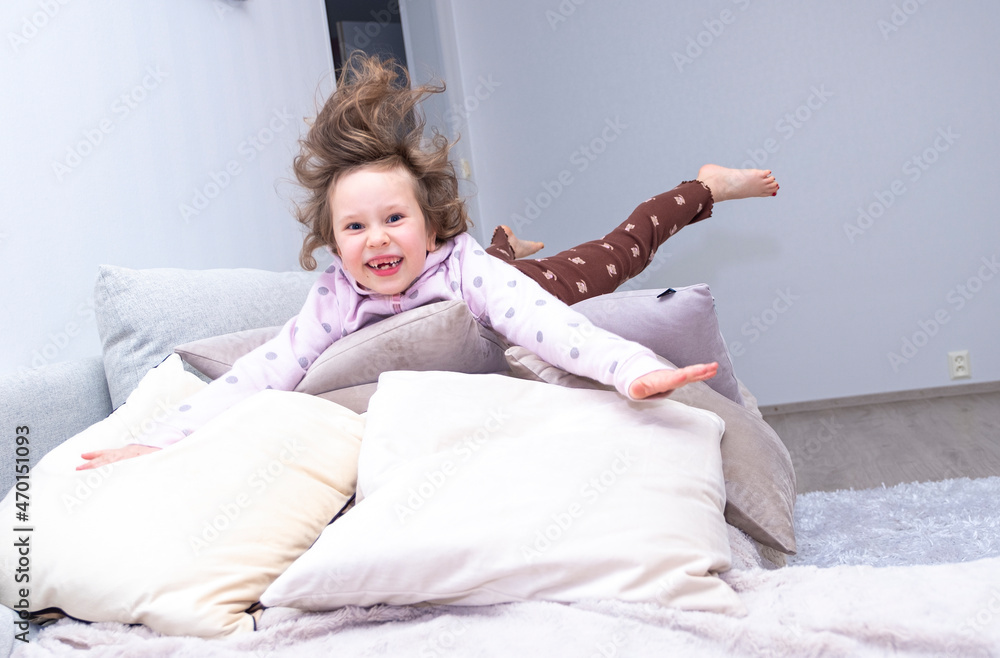 Caucasian girl cheerfully jumping on a soft sofa. The child smiles and ...