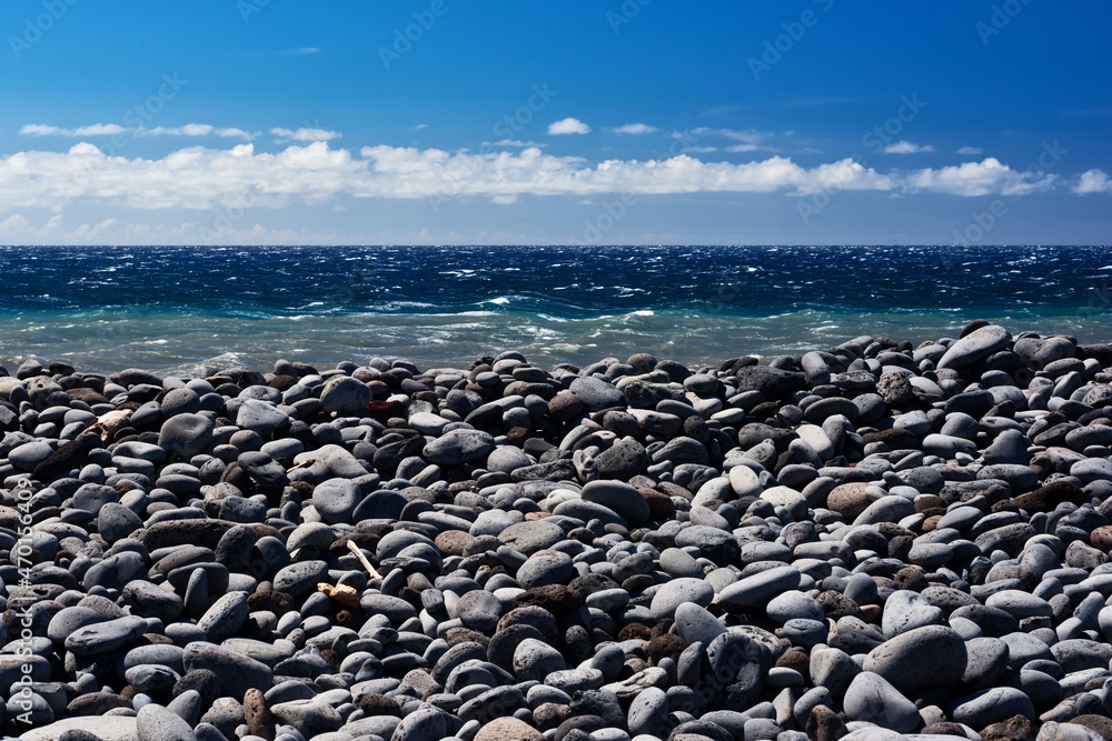 Lava rocks pile up along the high tide line of a small beach to meet ...