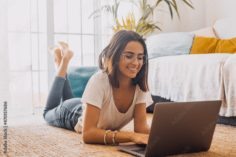 Happy young woman in eyeglasses typing using laptop while lying down on ...