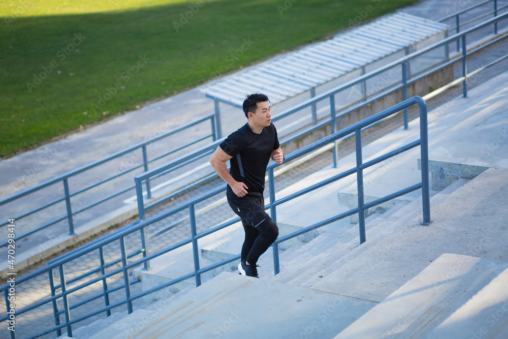 Asian male runner running around modern urban stadium up stairs Cardio ...