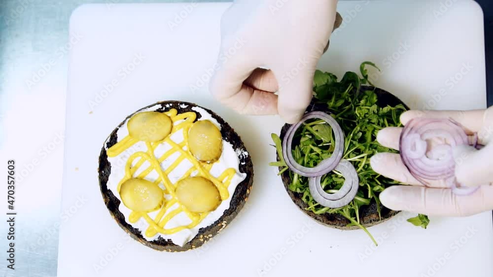 Culinary procedure of making tasty black burger. Chef puts onion rings ...