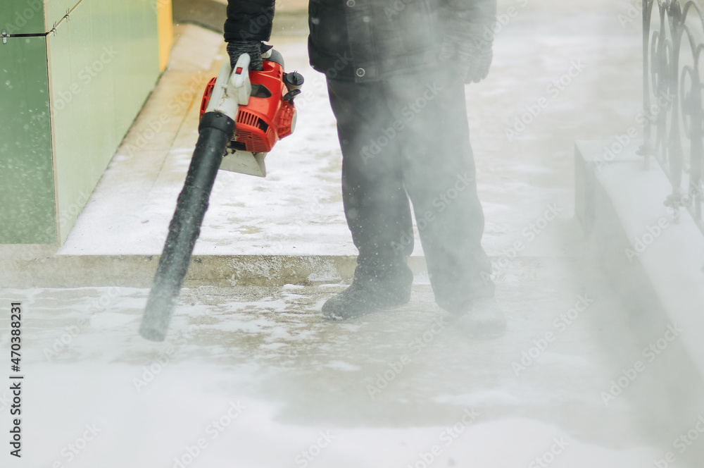 A man removes snow from the sidewalk with a wind blower. Lumps of snow ...