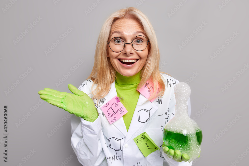 Positive blonde female researcher raises palm holds glassware with ...
