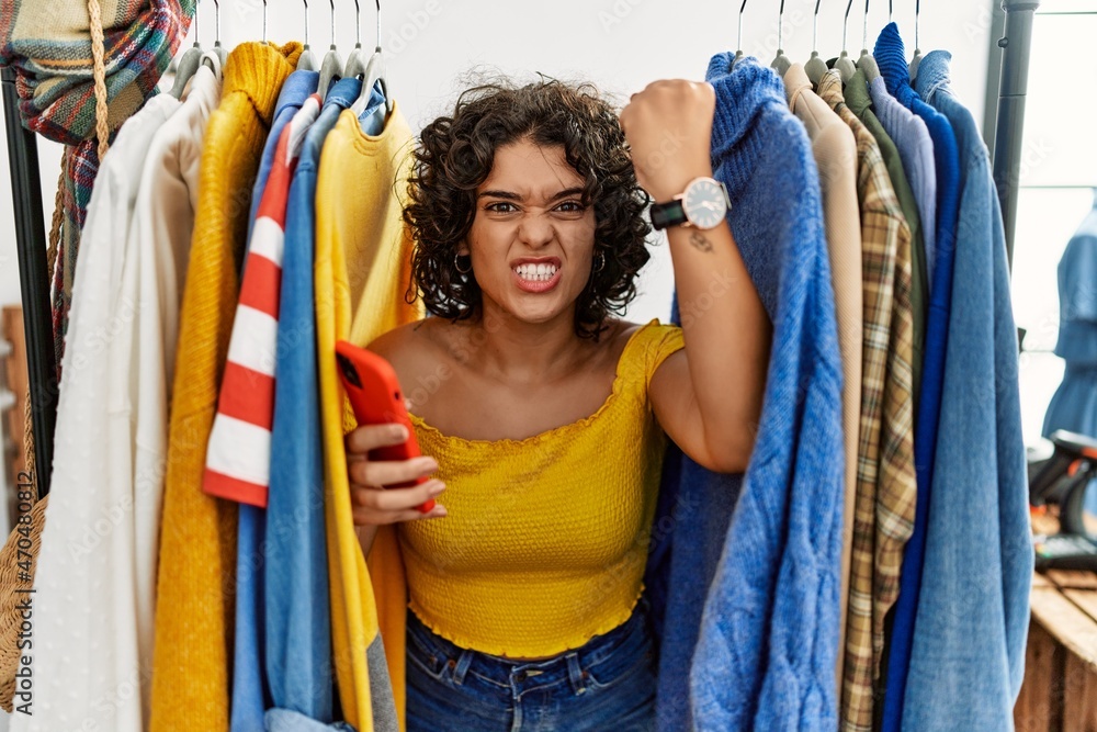 Foto de Young hispanic woman searching clothes on clothing rack using ...