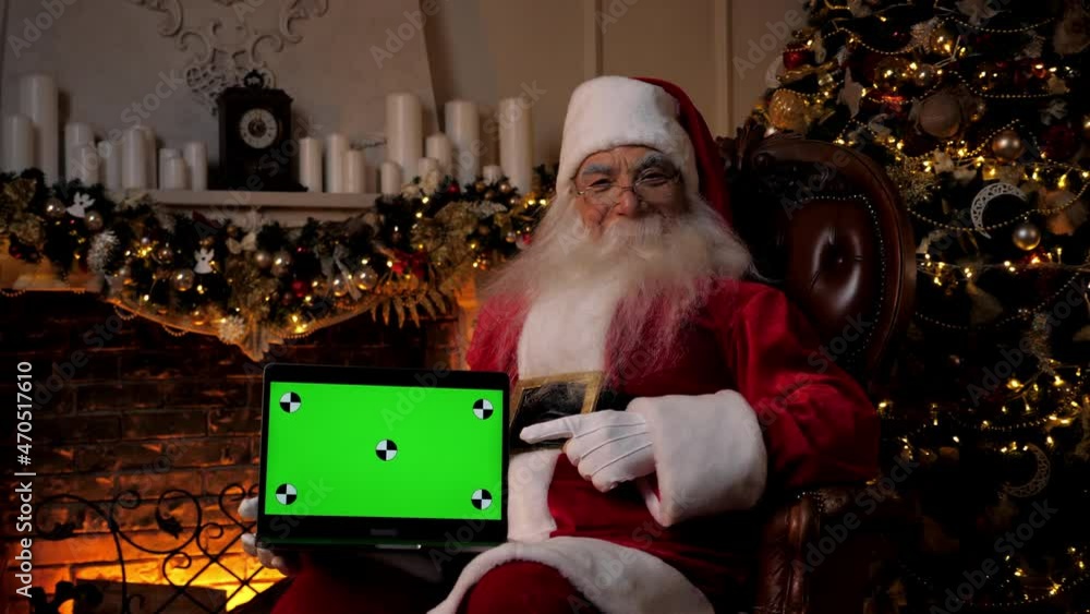 Modern smiling Santa Claus points finger at laptop green screen markers ...
