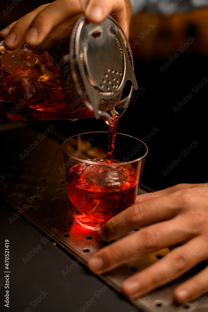 process of pouring a cocktail from a mixing cup with strainer into a ...