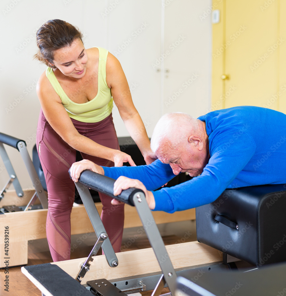 Foto de Young woman professional pilates instructor helping aged man ...