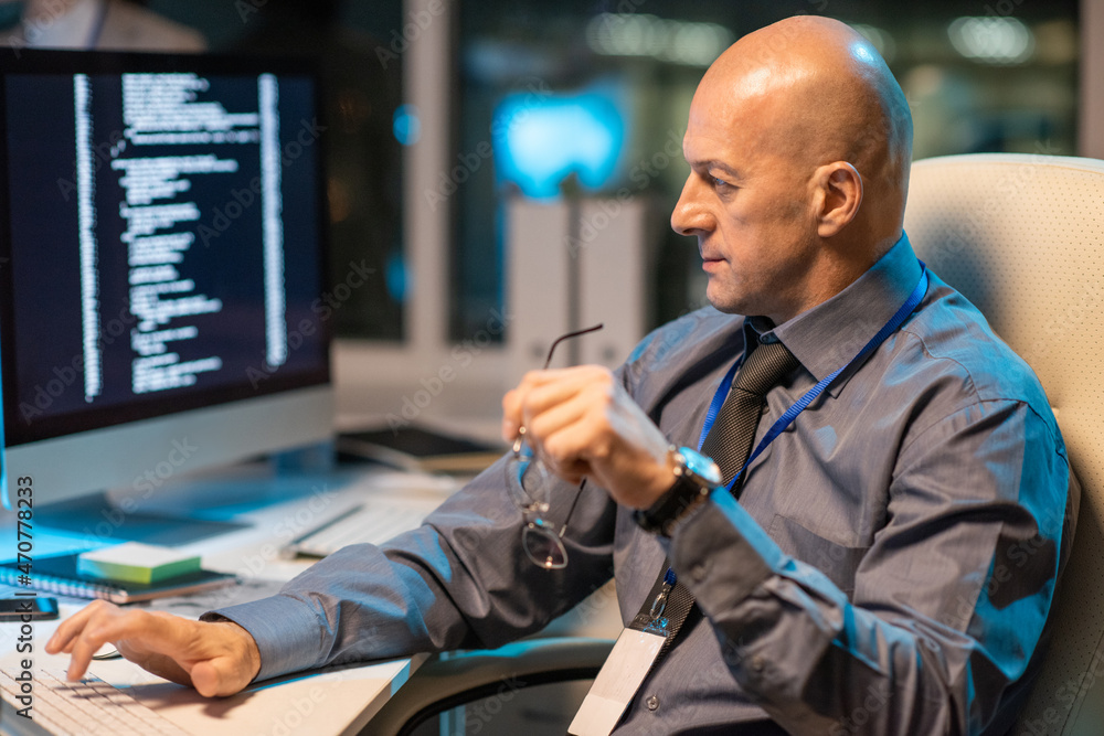 Mature bald it-engineer working in front of computer monitor while ...