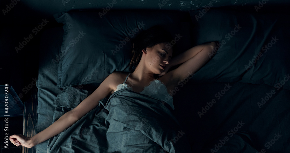 Brunette woman lying sound asleep in bed, changing position. A young ...