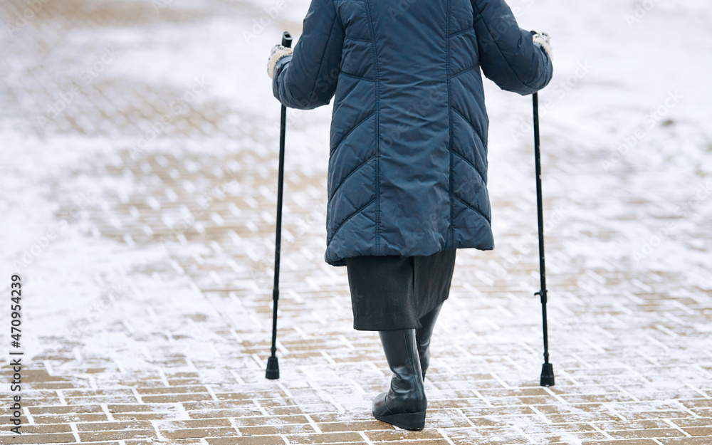 Old woman with walking canes in hands walks along snowy walkway in ...