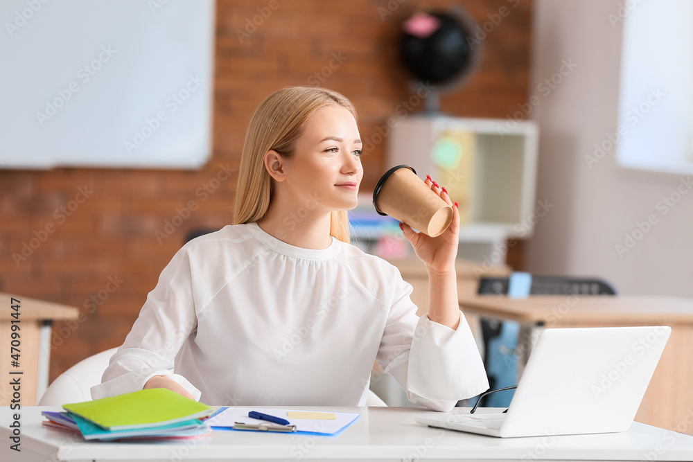 Young female teacher drinking coffee at desk in classroom Stock Photo ...