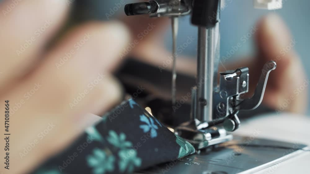 Women's hands raise foot of sewing machine and pull fabric by threads ...