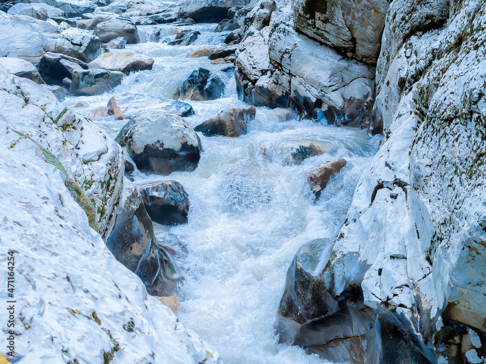 A turbulent foamy river flows over large rocks in a rocky gorge. Canyon ...