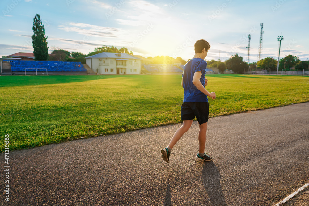 teen boy running along the stadium track, a soccer field with green ...