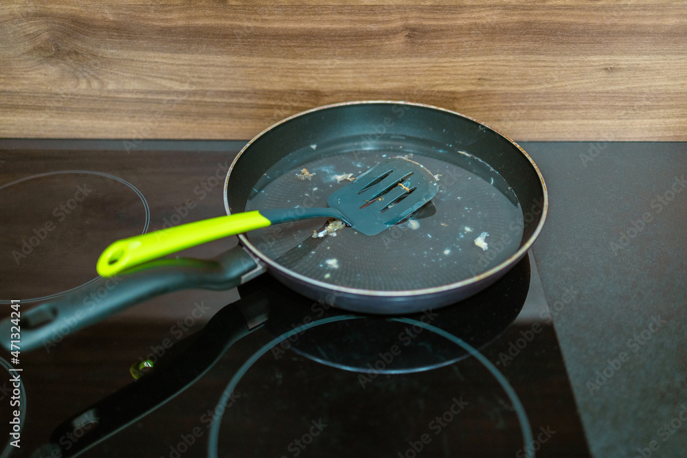 Dirty frying pan with plastic spatula on induction glass hob on modern ...