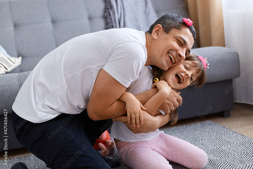 Cheerful little girl and attractive brunette man hugging each other ...