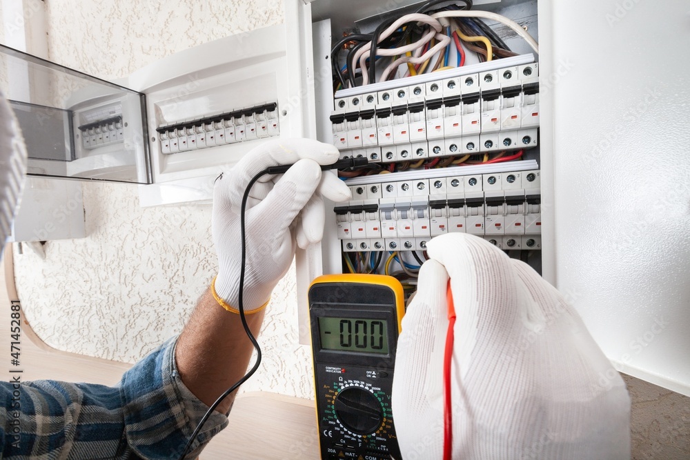 Electrician at work on an electrical panel protected in safety goggles ...