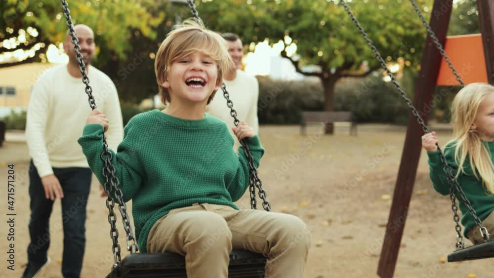LGBT family - Happy kids and fathers fun swinging on swing at city park ...
