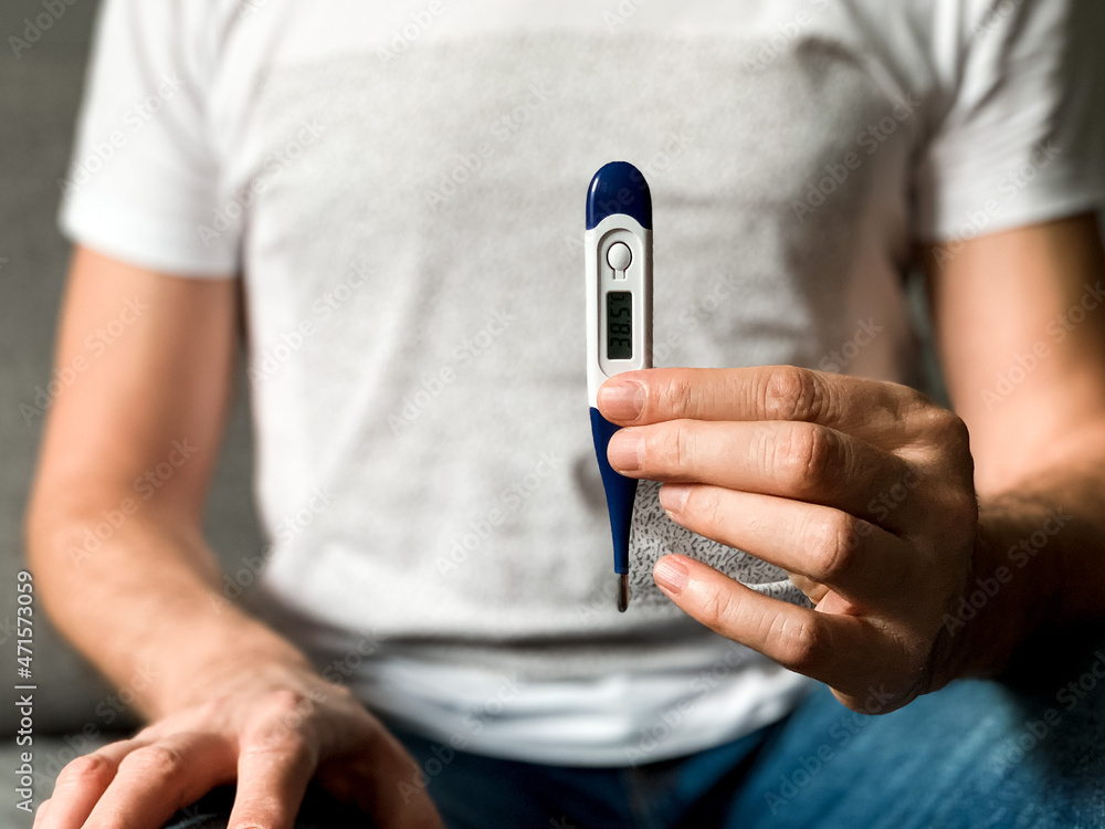 Man is checking temperature with digital thermometer. A man sitting on ...