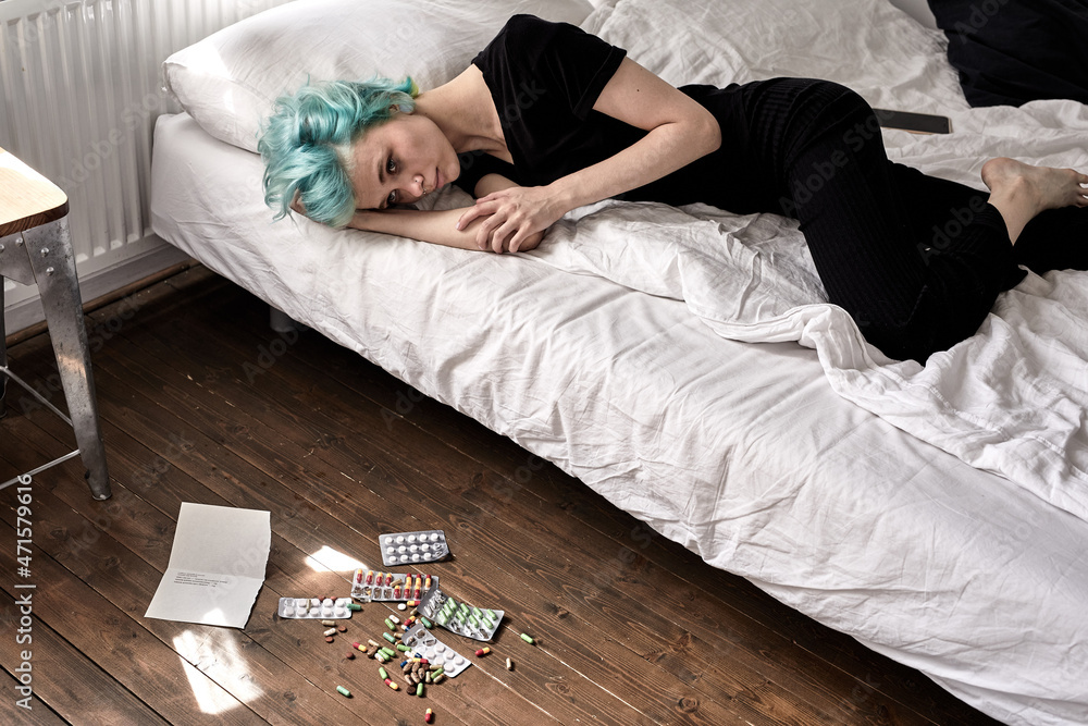 Suicide by medication overdose concept. pills on floor and young woman ...