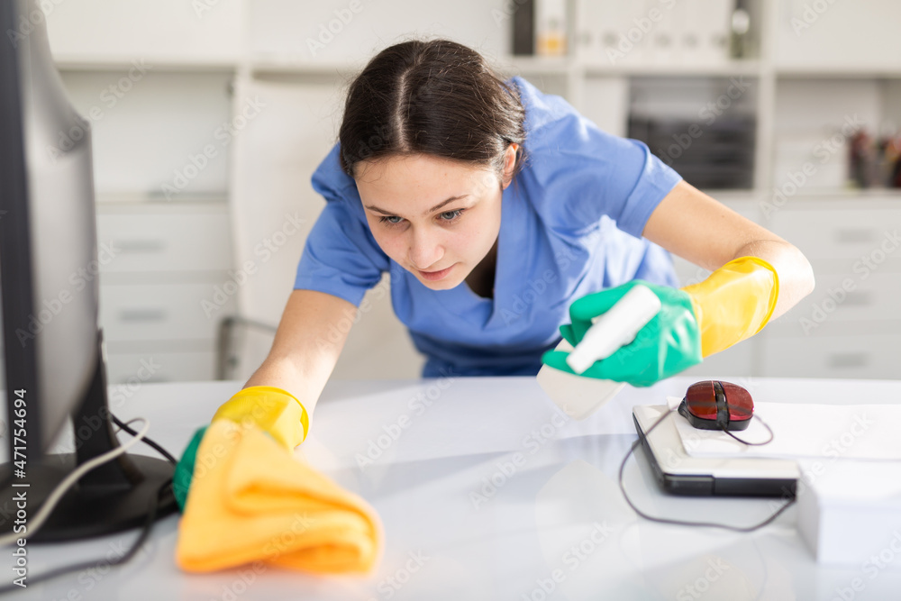 Young girl cleans up the desktop in the office with a rag and cleaning ...