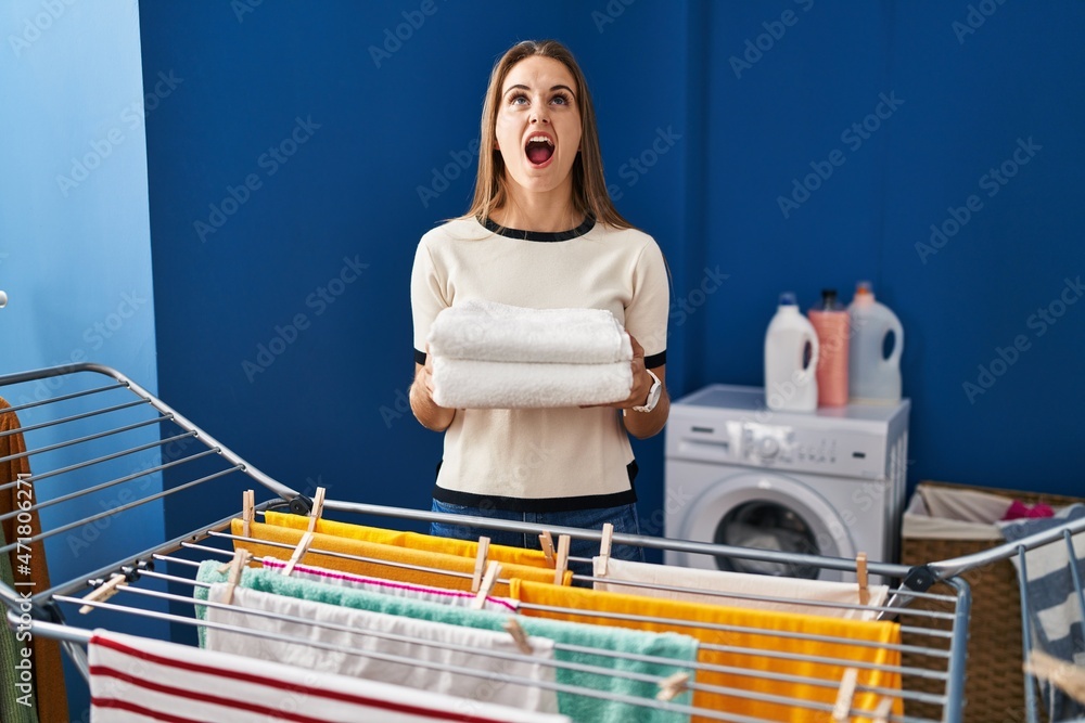 Young woman holding clean laundry from clothesline angry and mad ...