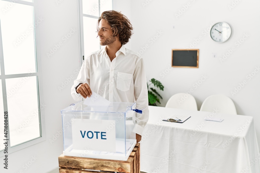 Young hispanic man voting putting envelop in ballot box looking to side ...