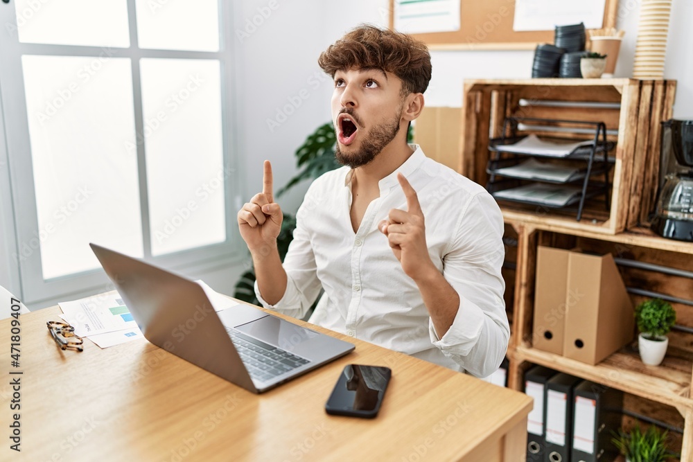 Young arab man working using computer laptop at the office amazed and ...