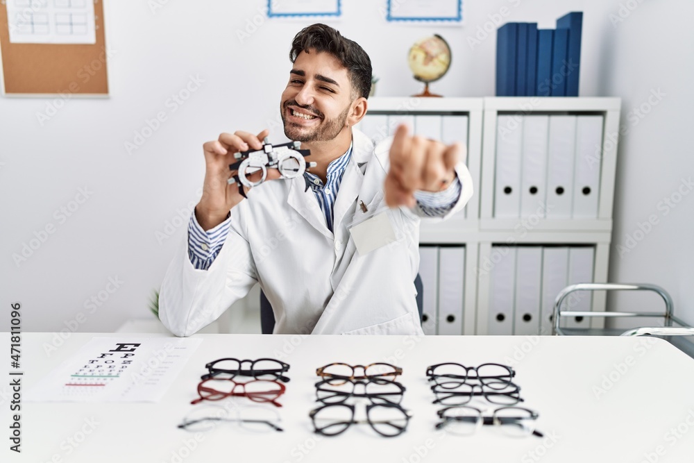 Young optician man holding optometry glasses pointing to you and the ...