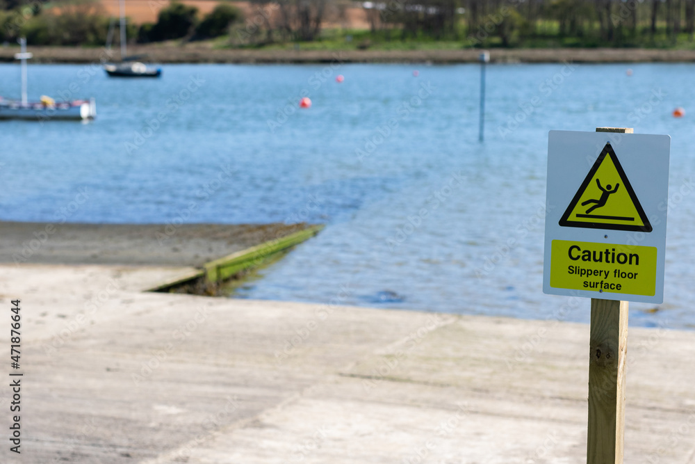 Warning sign for Slippery floor surface on a jetty by a river. The ...