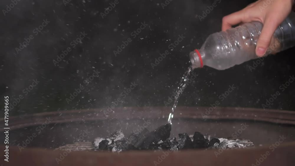 Man Extinguishing a campfire. Put out the fire with water from a bottle ...