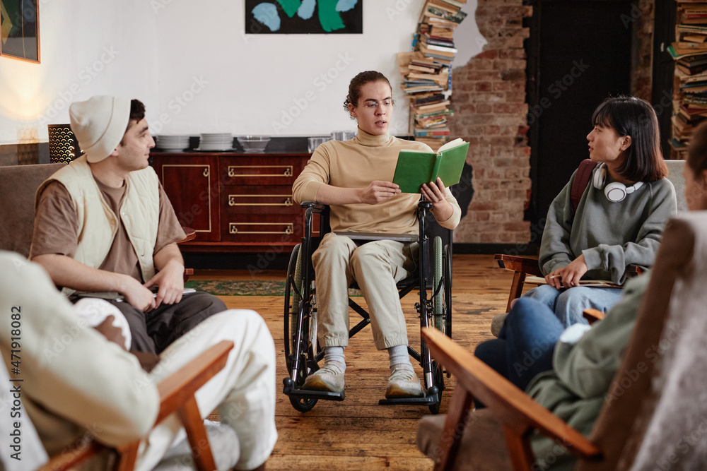 Teenage boy with disability reading a book for group of students during ...