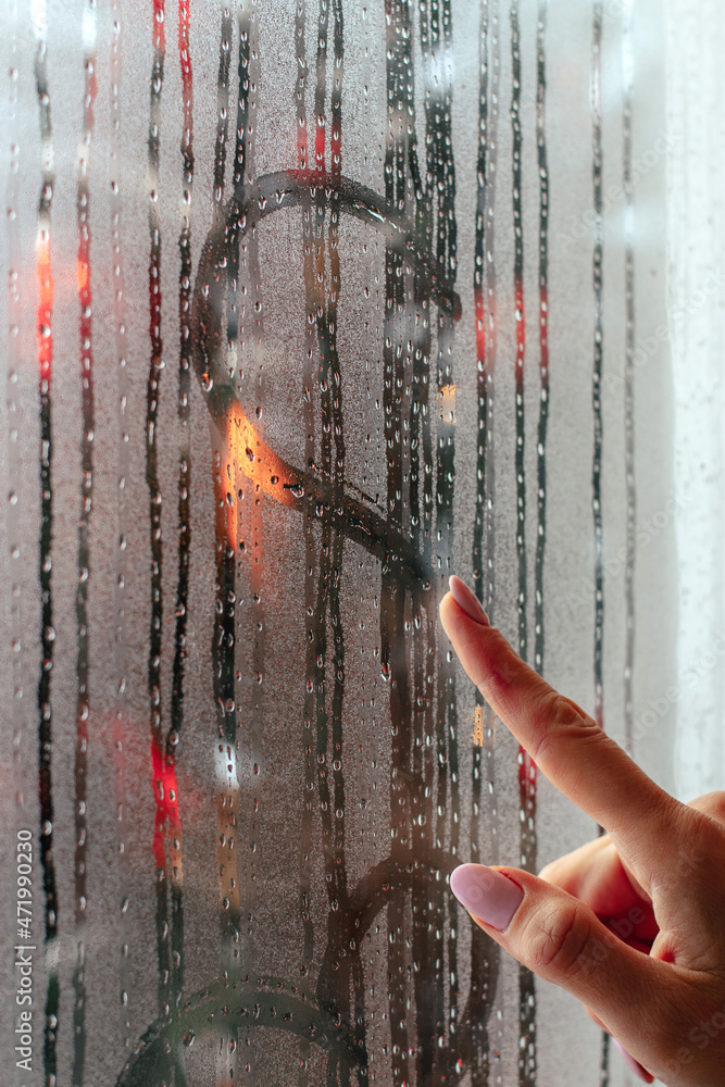 A woman draws a heart with her finger on a fogged window, a close-up of ...