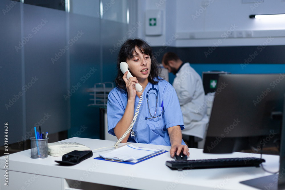 Medical assistant talking on landline phone for healthcare checkup appointment, working late ...
