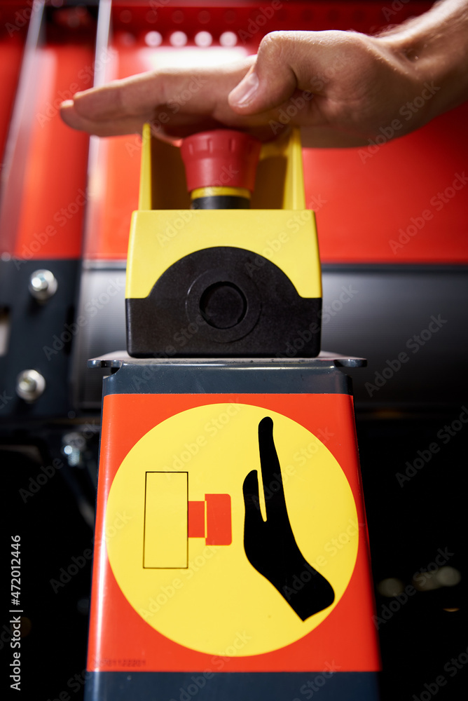 A man's hand touches a red emergency stop signal button, in production ...