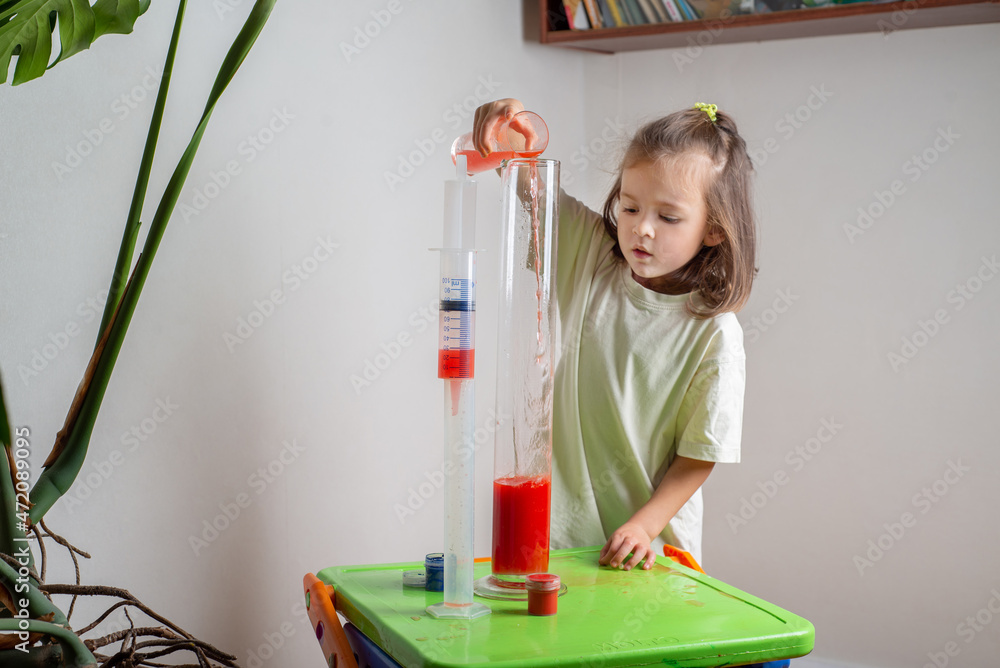 Child pours a colored liquid into a test tube while making a chemistry ...