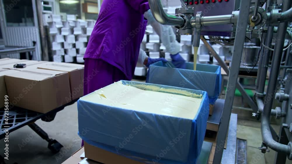 Milk factory worker in uniform spreading butter in the box. Big faucet ...