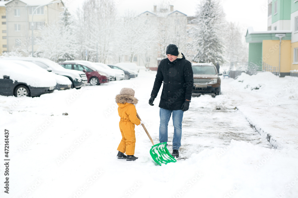A child helps his father to remove snow in the yard of the house in the ...