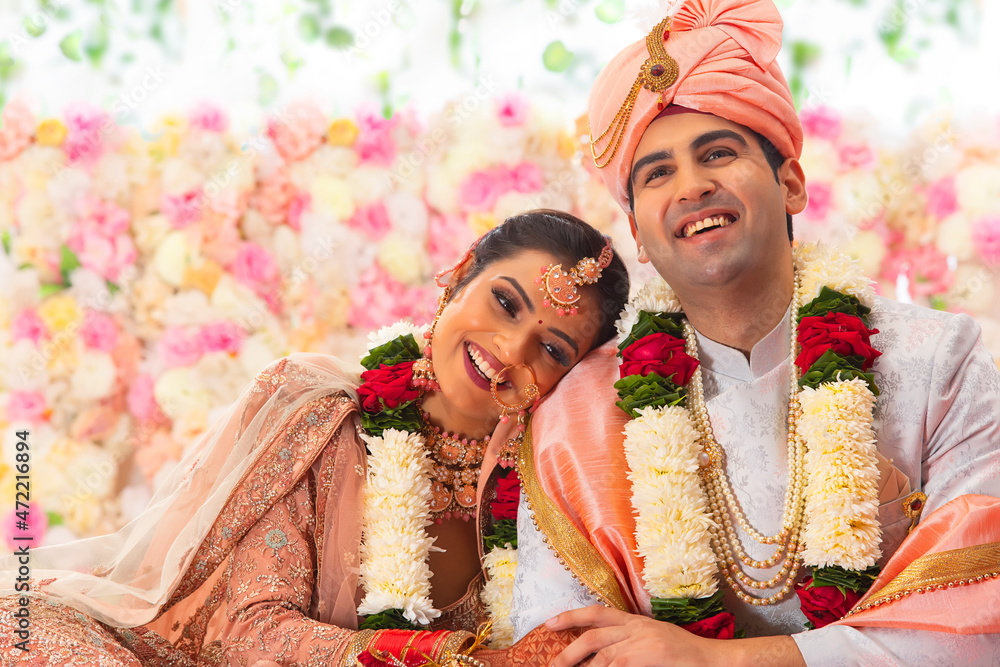 Portrait of a happy Indian wedding couple sitting together on mandap ...